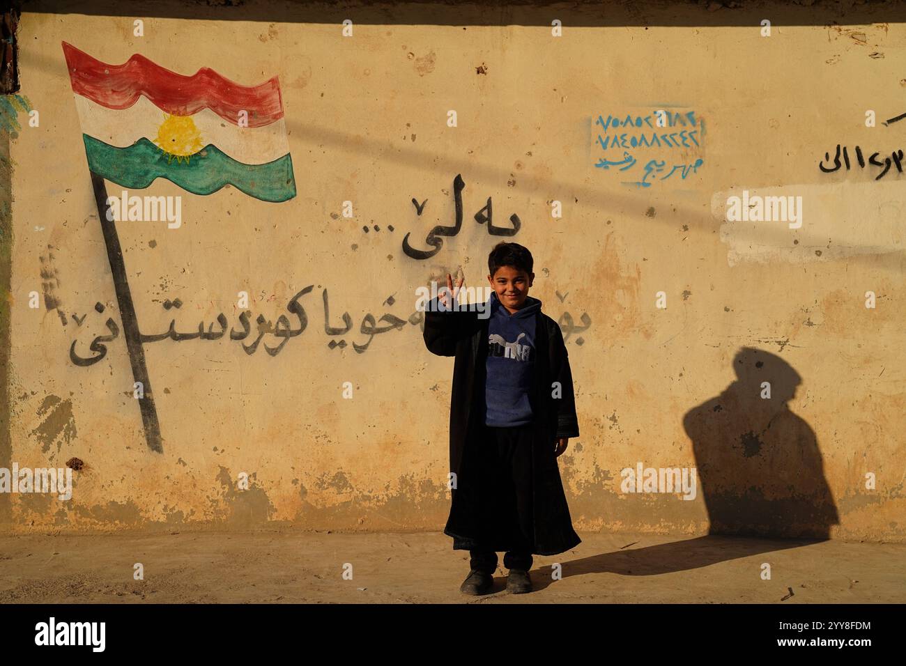 A boy stands infront of the Kurdish flag at Domiz camp for Syrian ...