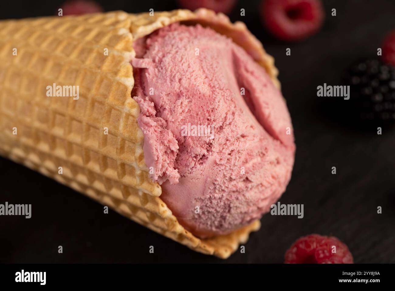 red raspberry ice cream in a waffle cone on a black background ...