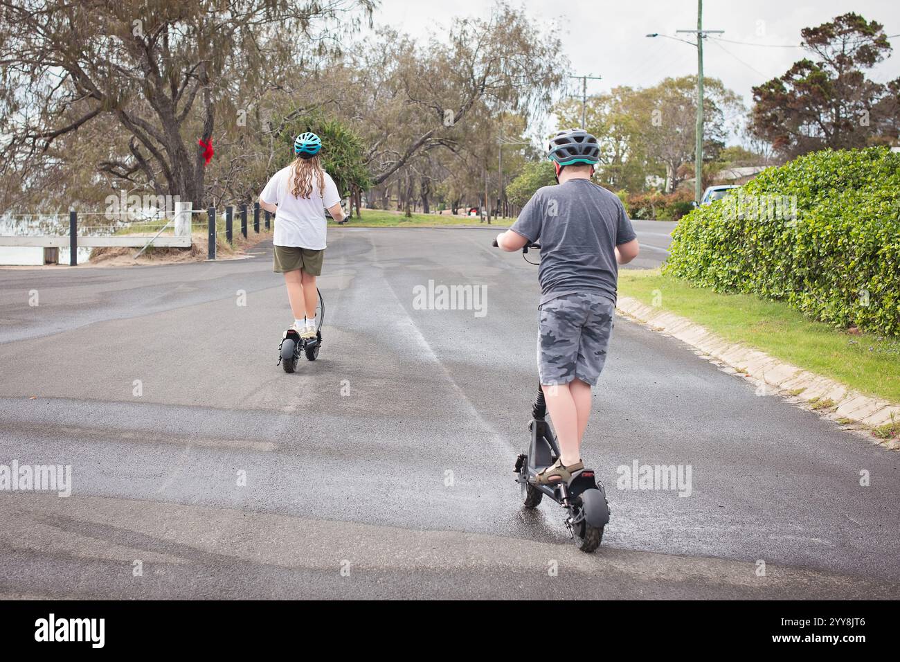pre teen kids on e-scooters wearing helmets paved road riding away ...
