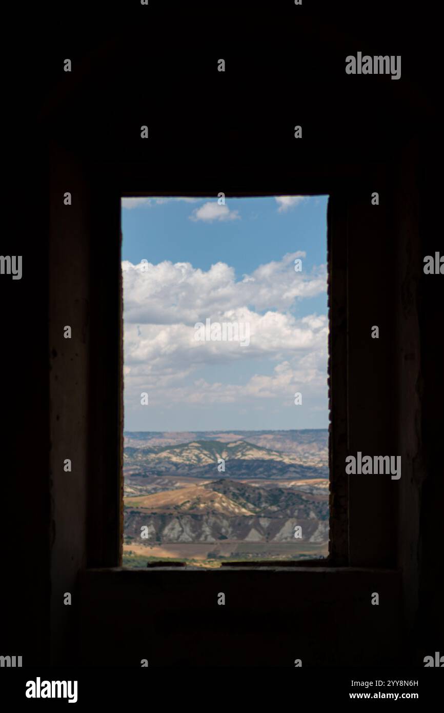 View through a rustic window framing rolling hills and a blue sky with ...