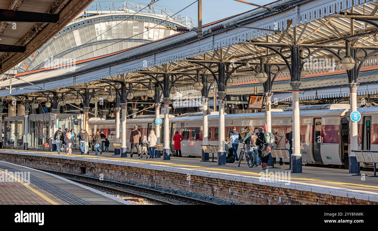 A crowd of passengers alight from a train and walk along a railway ...