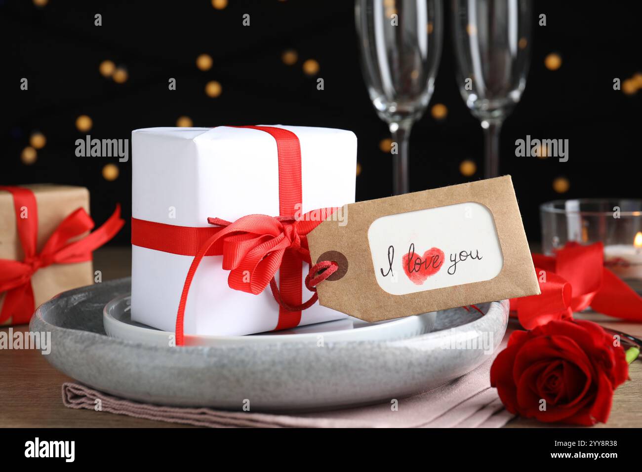 Beautiful place setting and tag with phrase I Love You on table against blurred lights, closeup ...