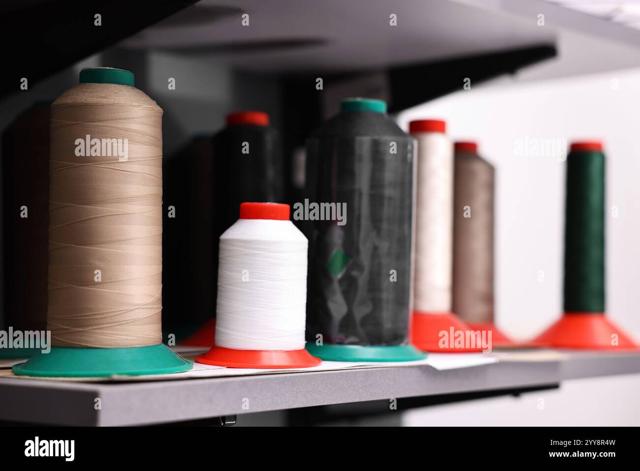 Many different spools of thread on white shelf in professional workshop ...