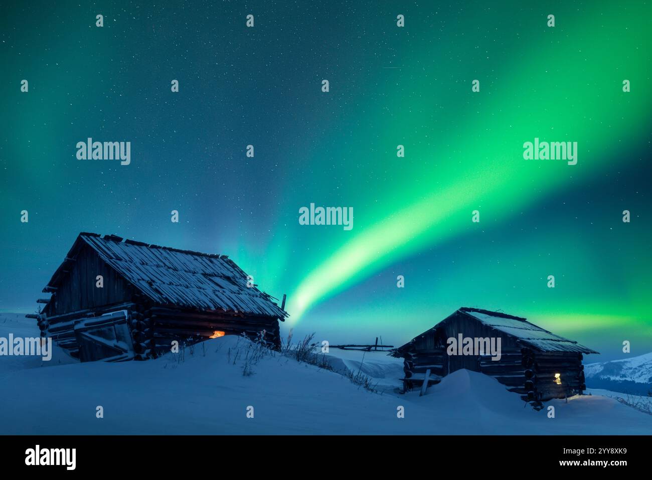Old wooden cabins in snowy mountains under incredible Northern lights ...