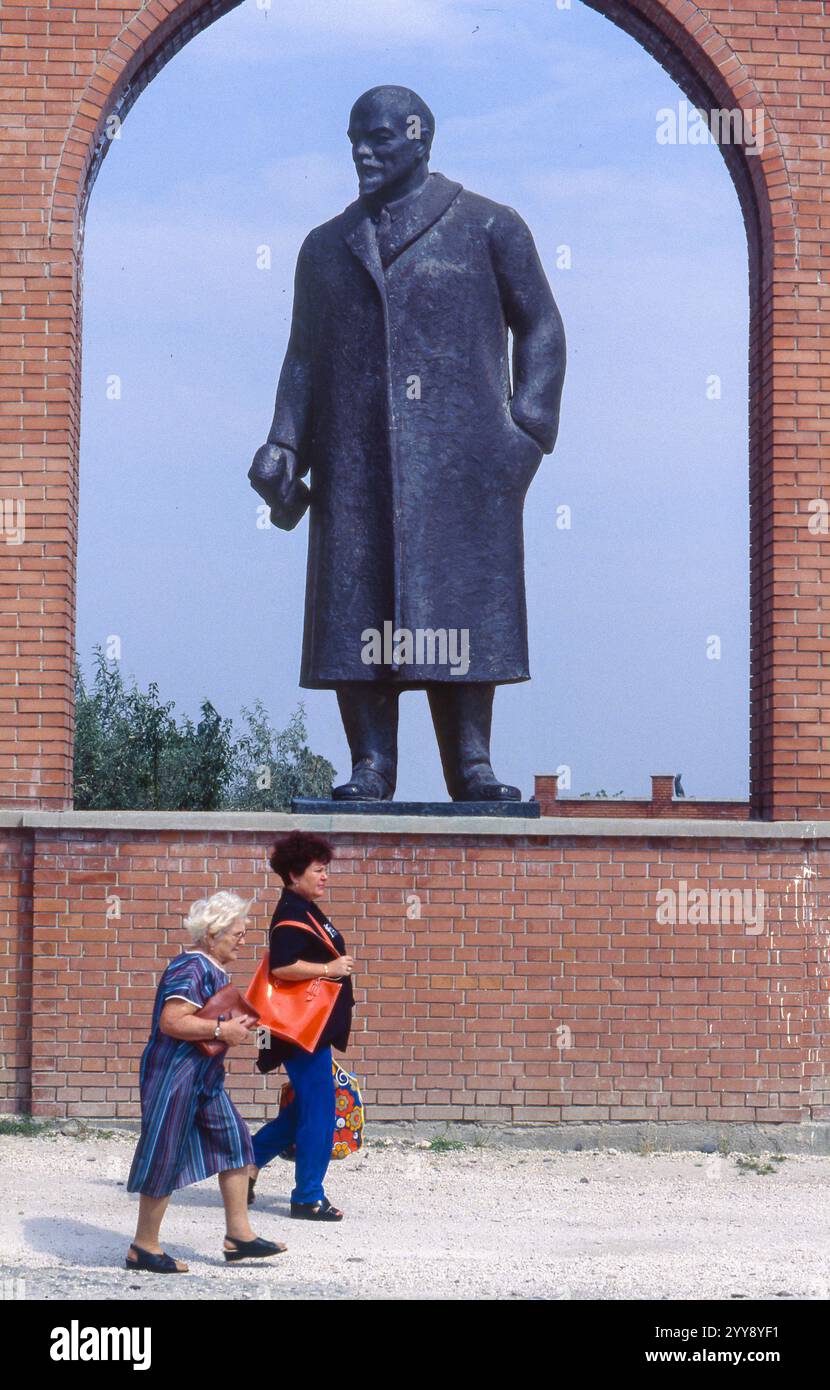 Hungary, Budapest, women pass a statue of Lenin in Memento Park or ...