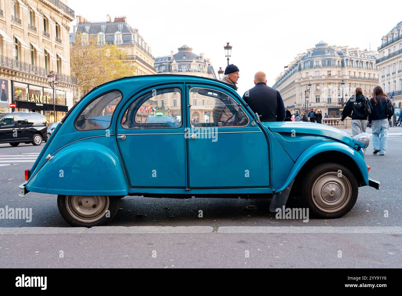 Classic blue car parked on a bustling street in Paris while pedestrians ...