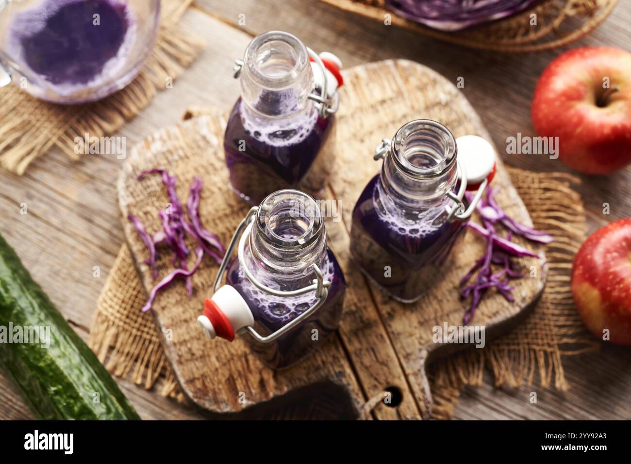 Purple cabbage juice in three glass bottles with red apples and ...