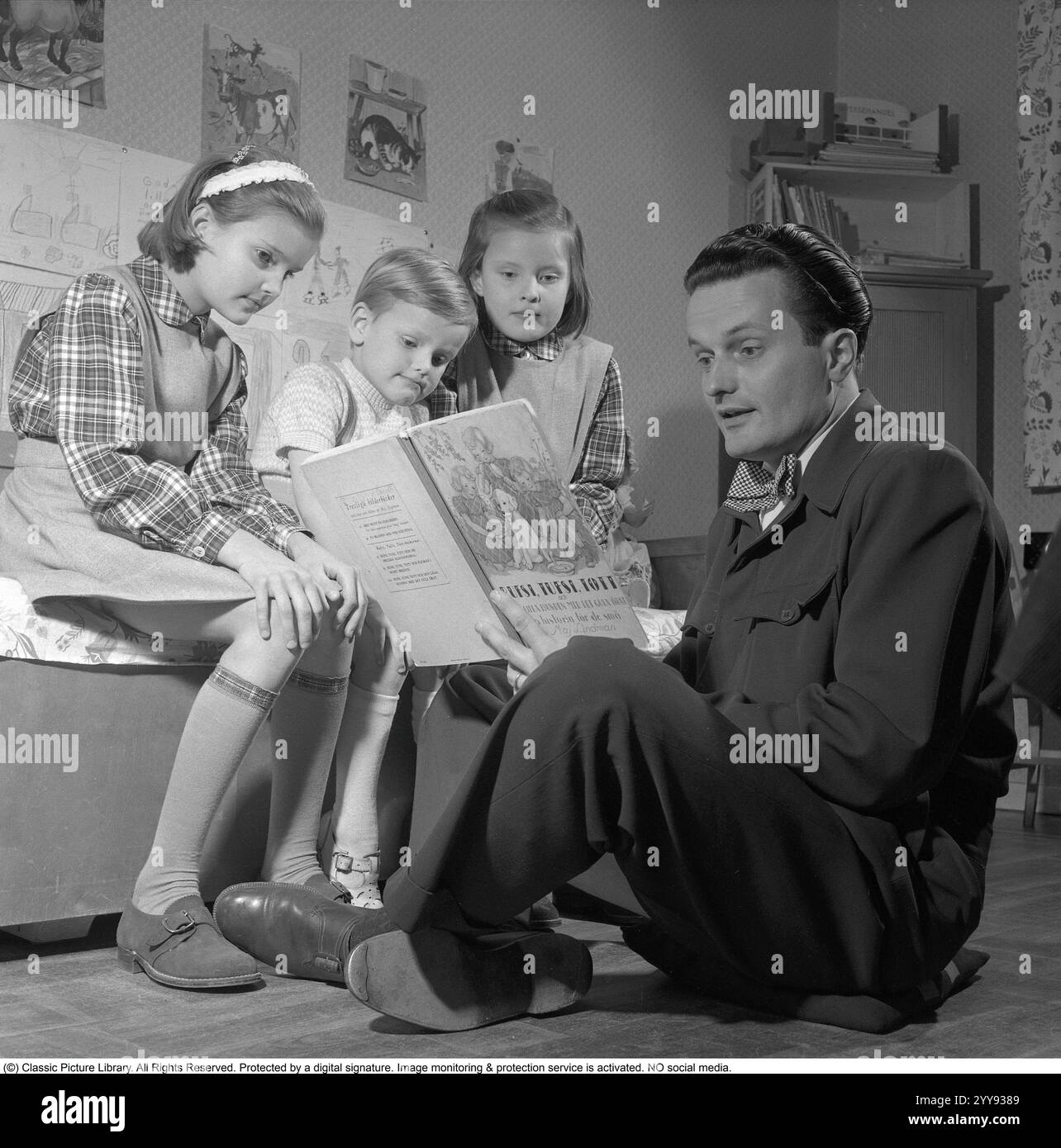 In the 1950s. A father reads from a book for his three children. He is ...