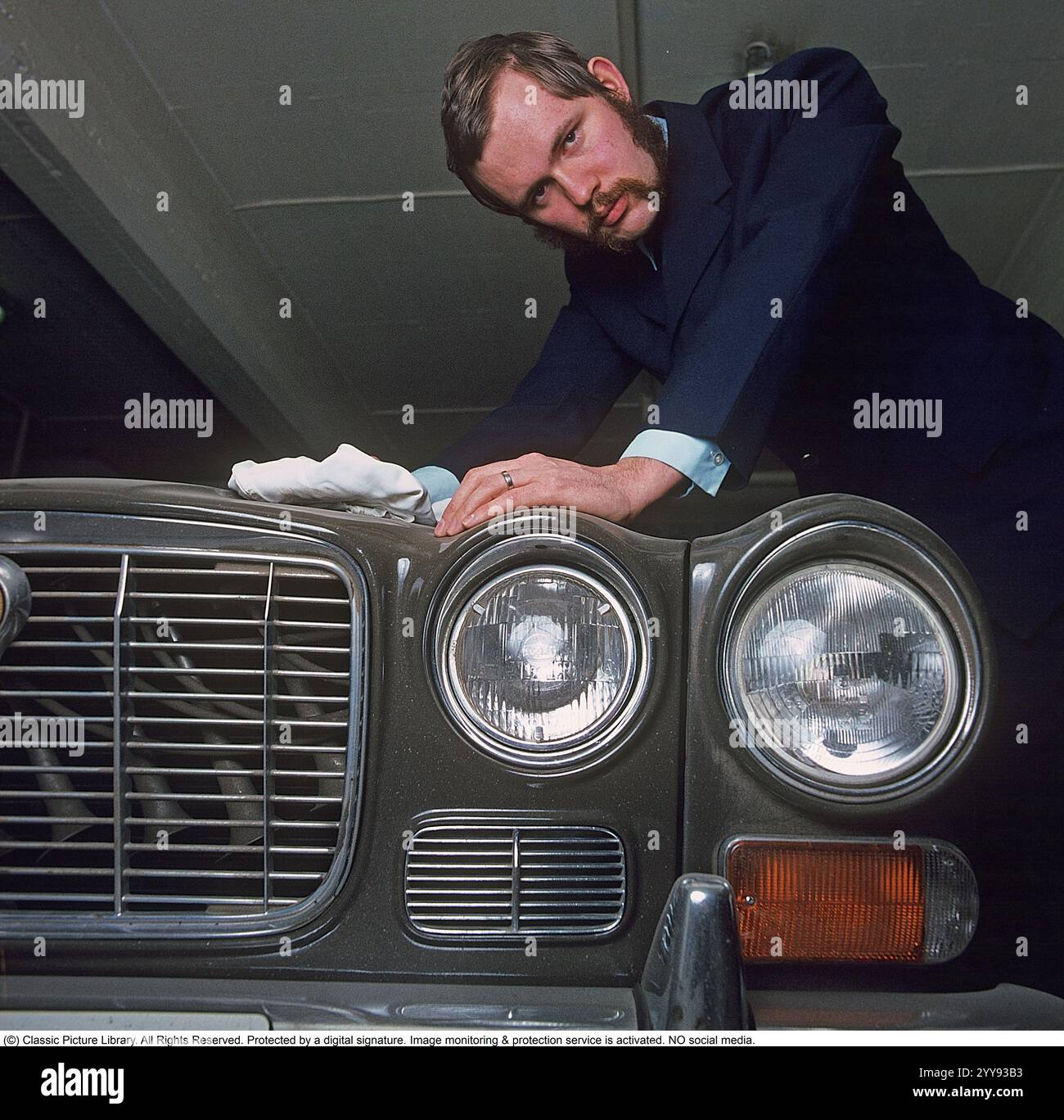 Man with a Jaguar car. He has a serious look on his face when polishing ...