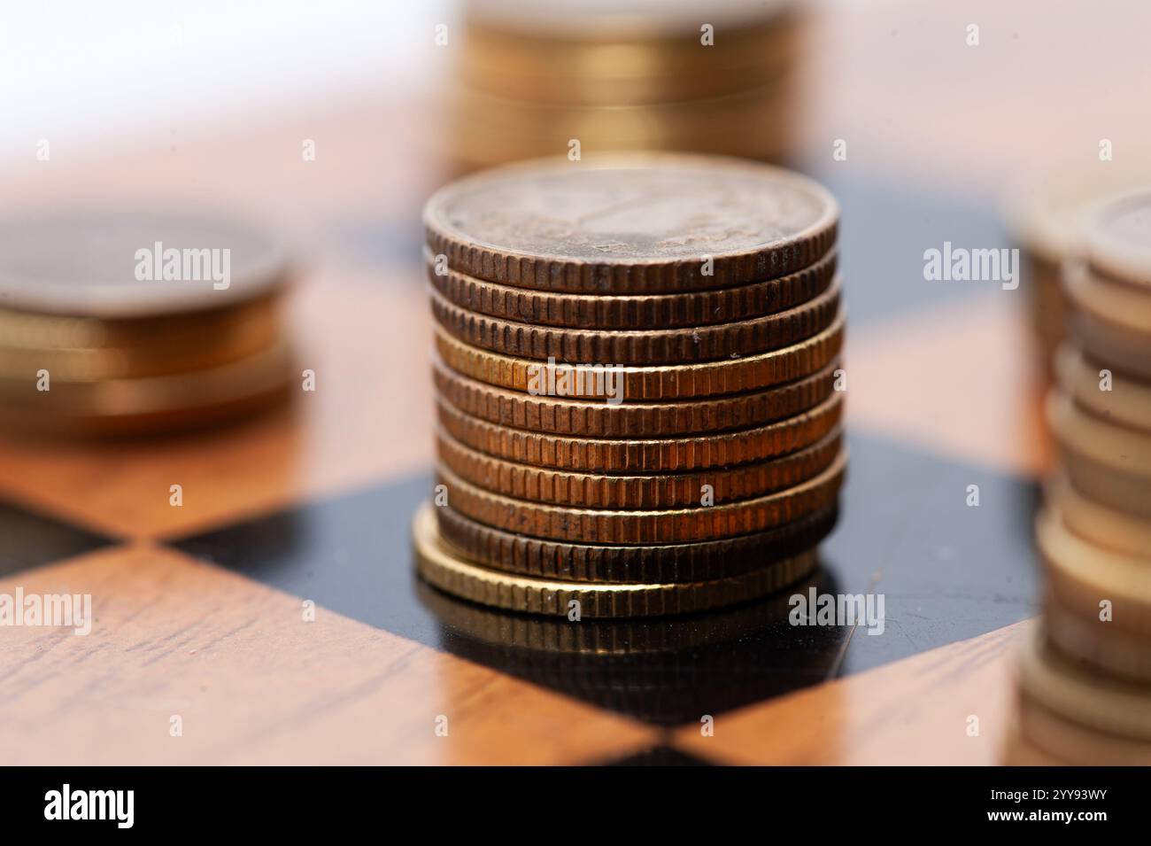 A stack of coins on a wooden chess board. The coins are gold and silver ...