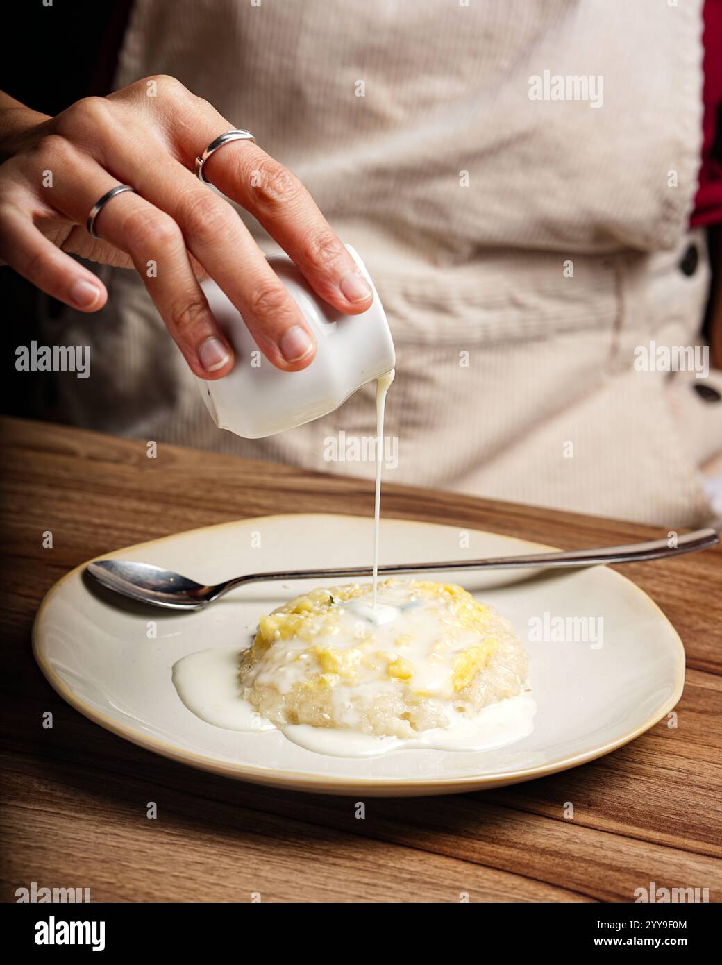 A close-up of Thai mango sticky rice being drizzled with rich coconut ...