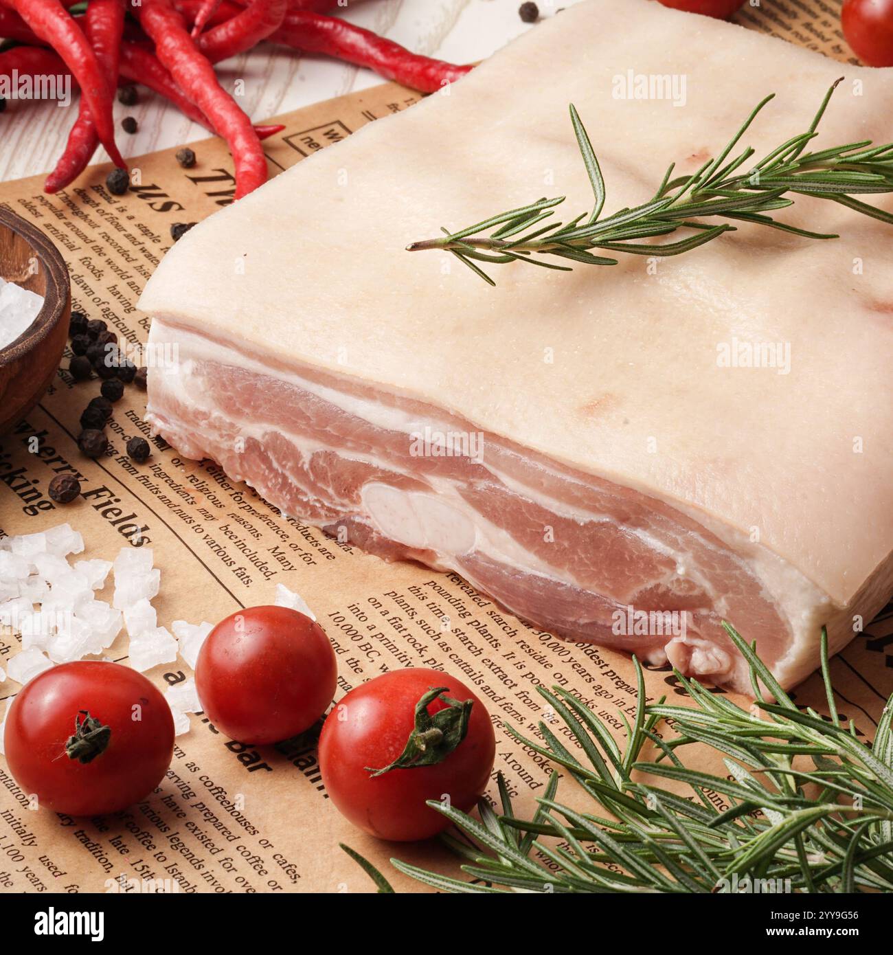 Fresh raw pork belly slab with skin-on, garnished with rosemary, cherry ...