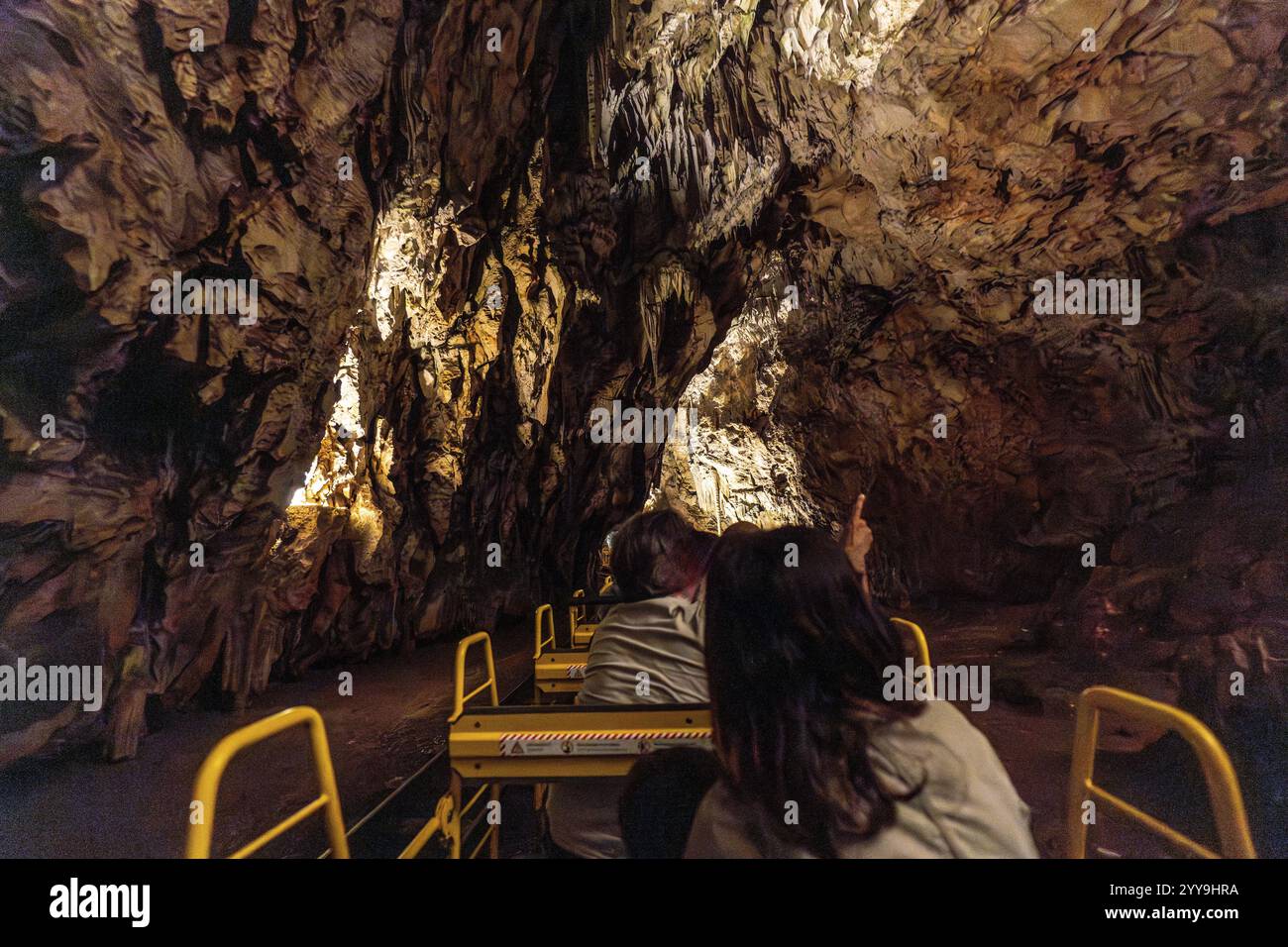Tourists riding a train inside postojna cave, illuminated by electric ...