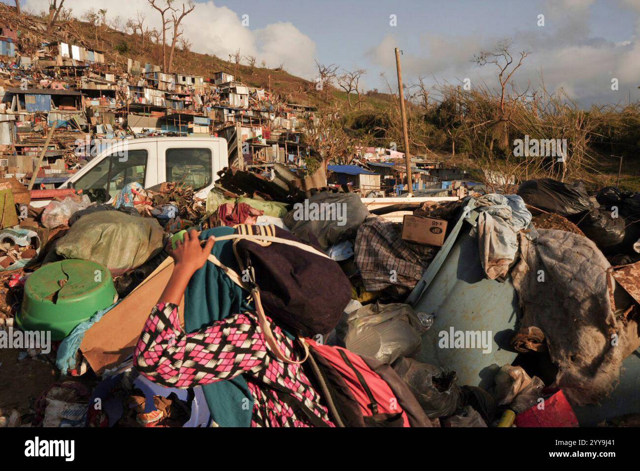 A woman carrying her belongings walks past debris after Cyclone Chido ...