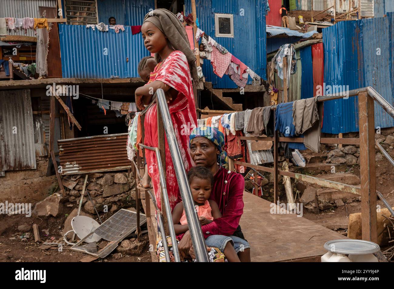 Women rest on a footbridge over a stream filled with debris in the ...