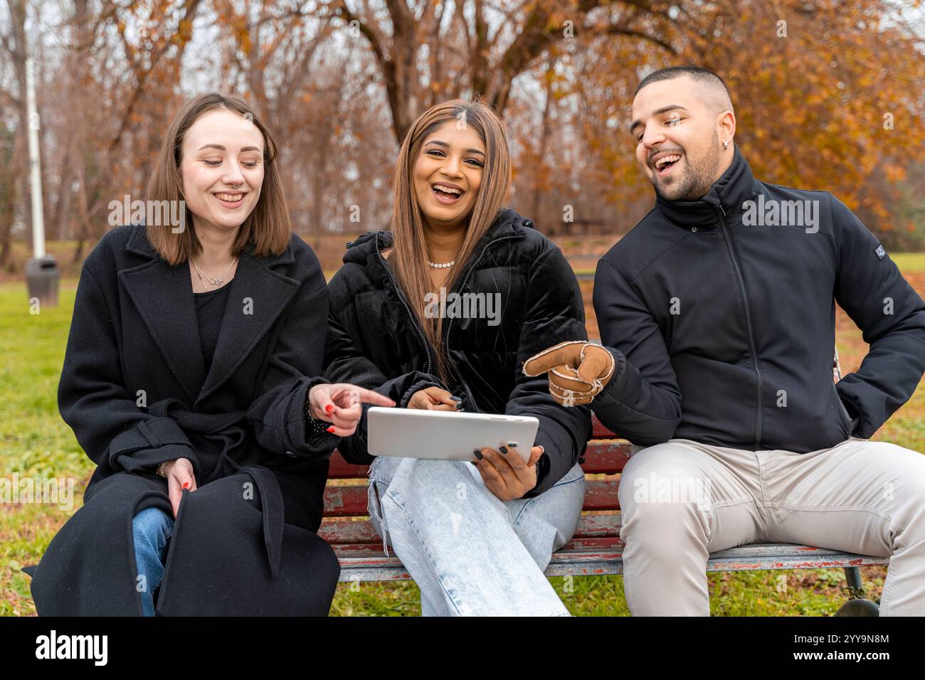 three young male and female friends using tablet having fun sitting on ...