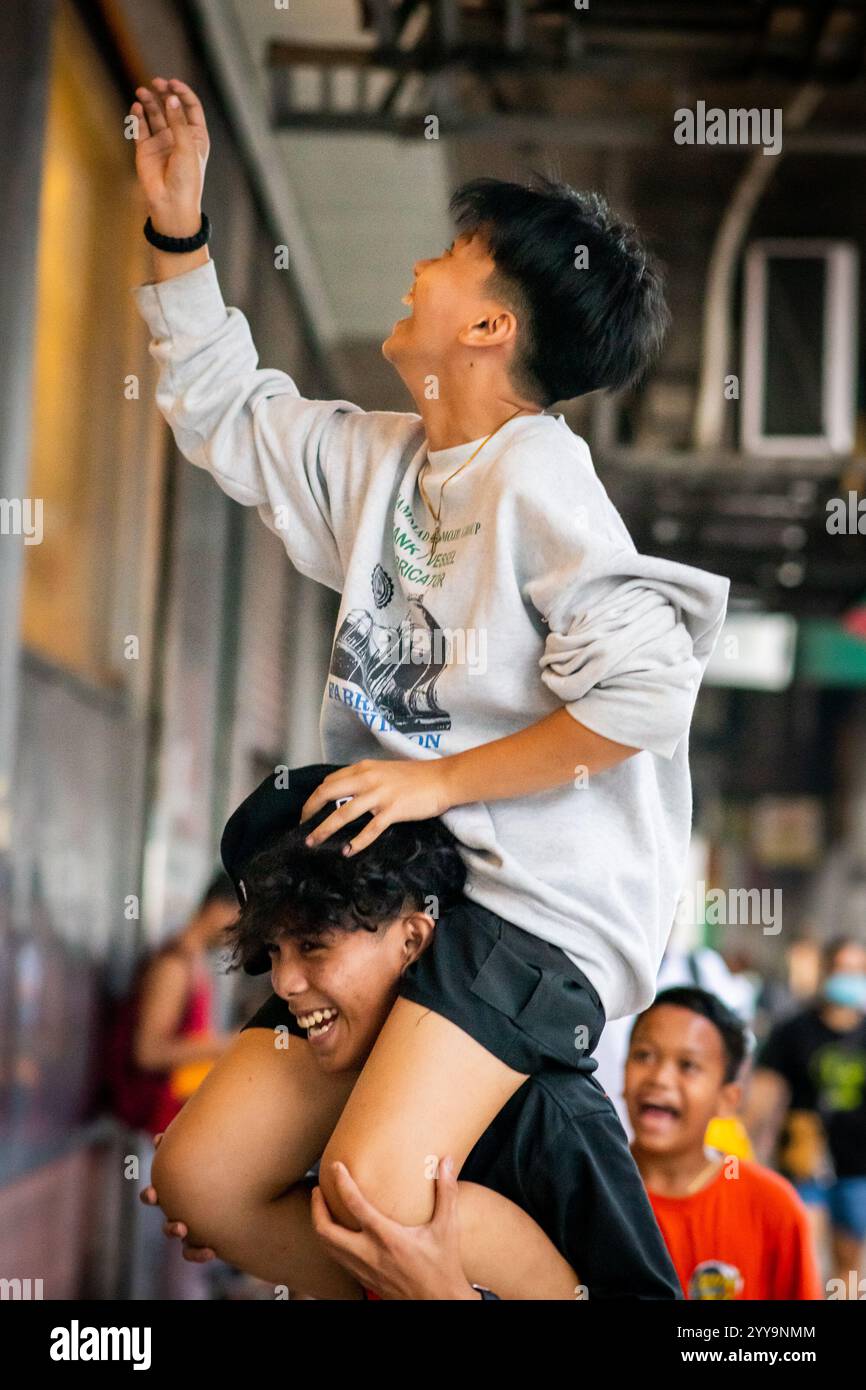 Filipino boys struggle to get their ball down from a high wall. They are playing on the streets ...
