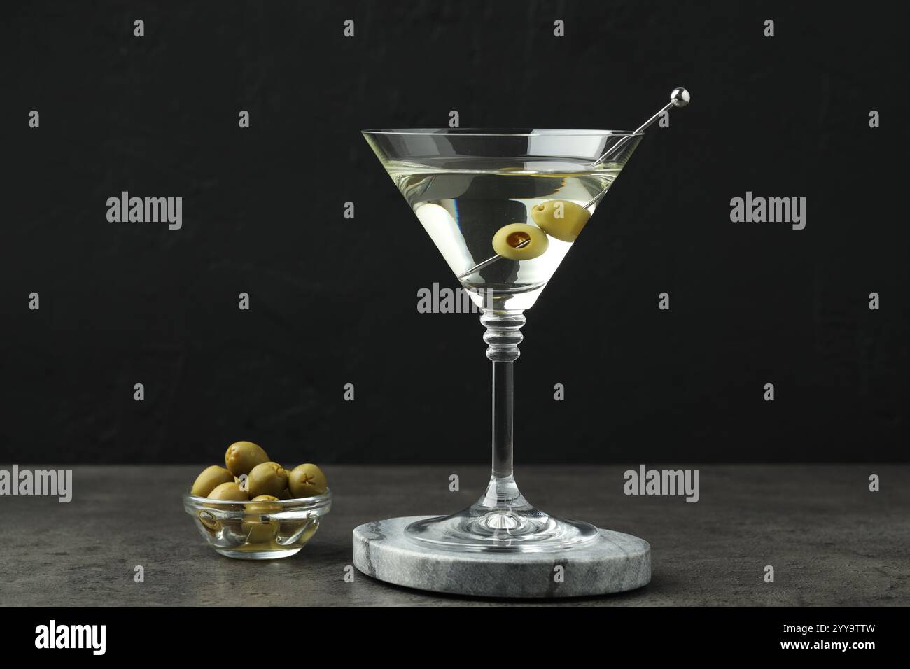 Martini cocktail with olives in glass on grey table against black ...