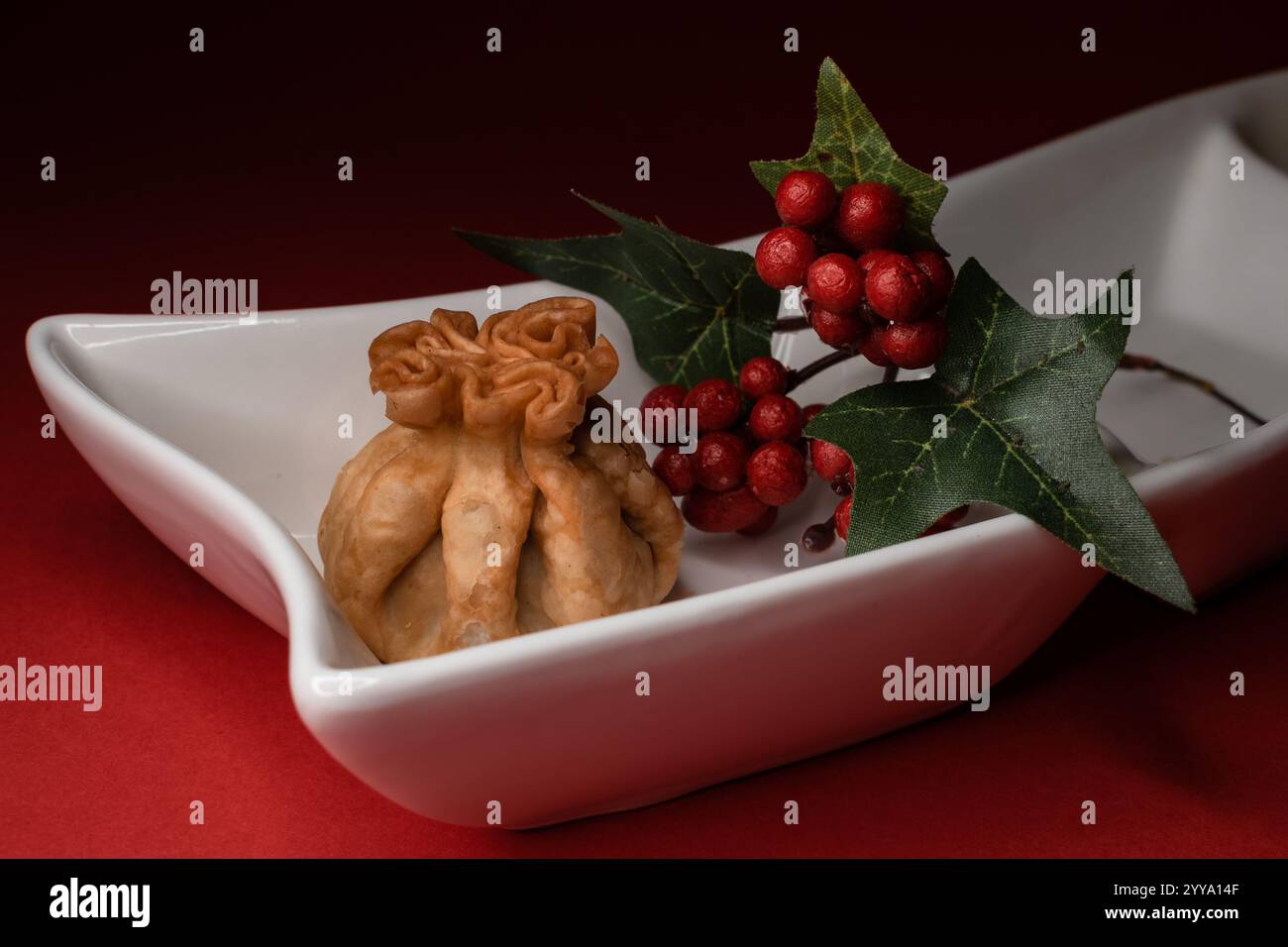 Single wonton dumpling with mistletoe, white plate on gradient burgundy ...