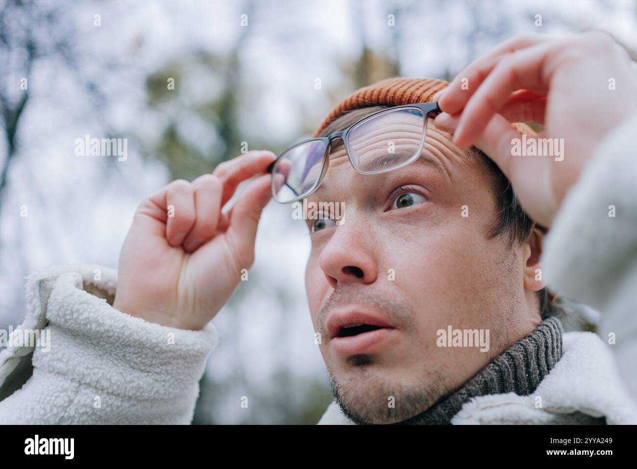Shocked man with glasses and beanie looking up with surprised ...