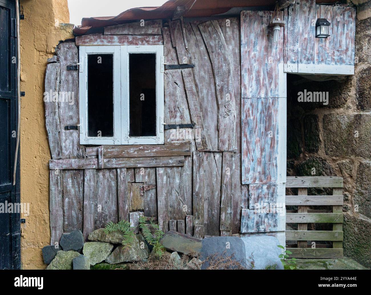 Wooden facade of a dilapidated hut with a window and a door. The door is open and the window is ...