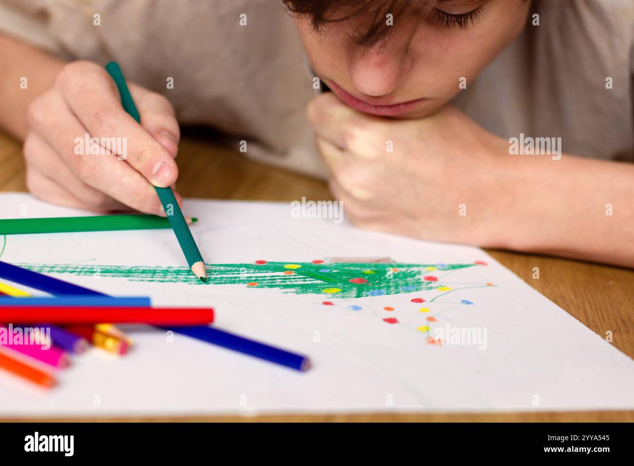 Sad teenage boy lying on the floor draws a Christmas tree with colored ...
