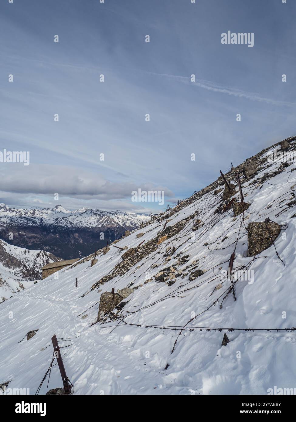 A rugged snowy mountain slope featuring remnants of a barbed wire fence ...