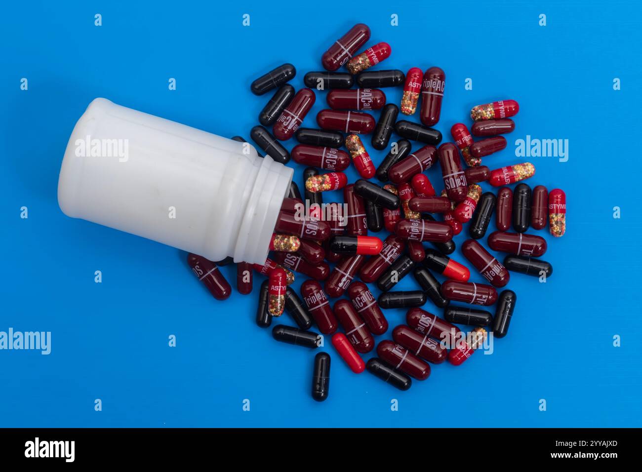 A white plastic bottle with red and black medicine capsules scattered ...
