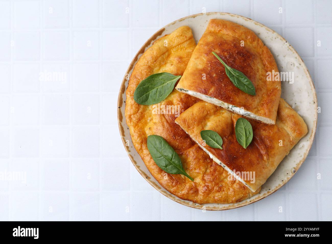 Tasty calzones with basil and cheese on white tiled table, top view ...