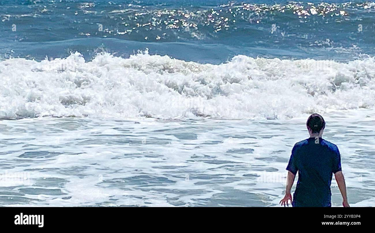 Individual wades in the ocean's shallow water while large waves crash ...