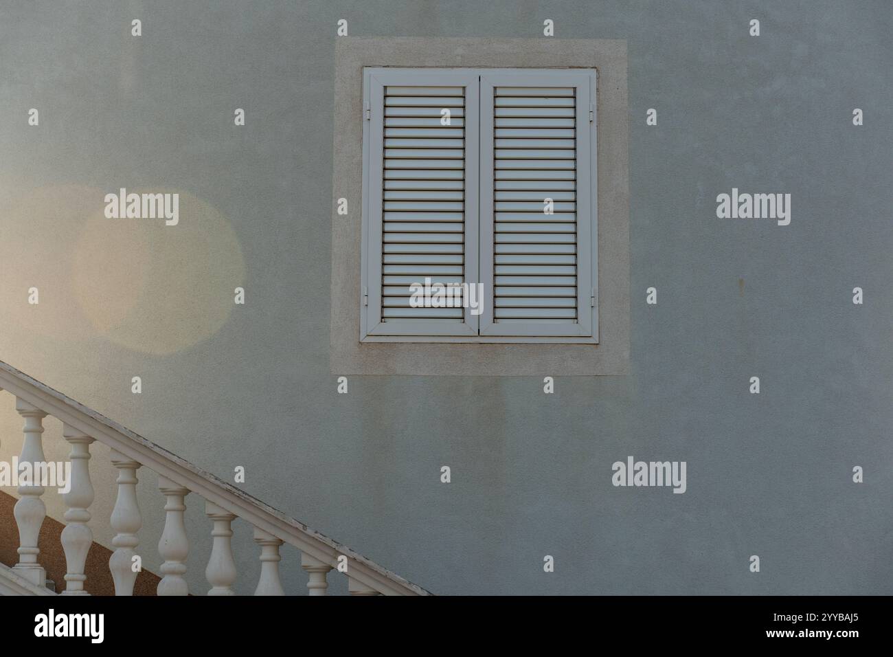 Closed white wooden shutters on window of textured light blue wall with ...