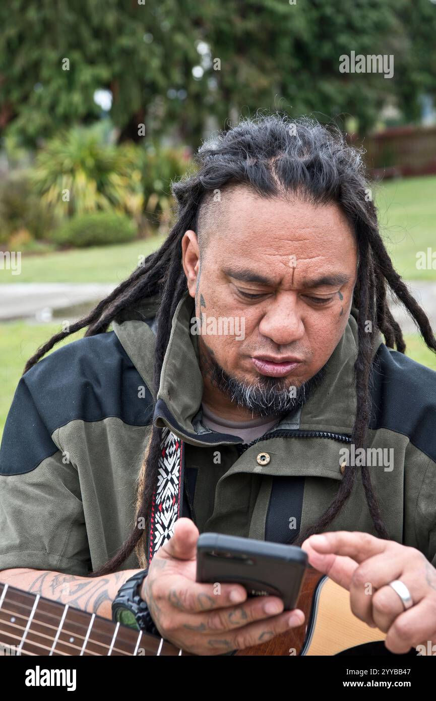 Maori man with guitar and using cell phone Stock Photo - Alamy