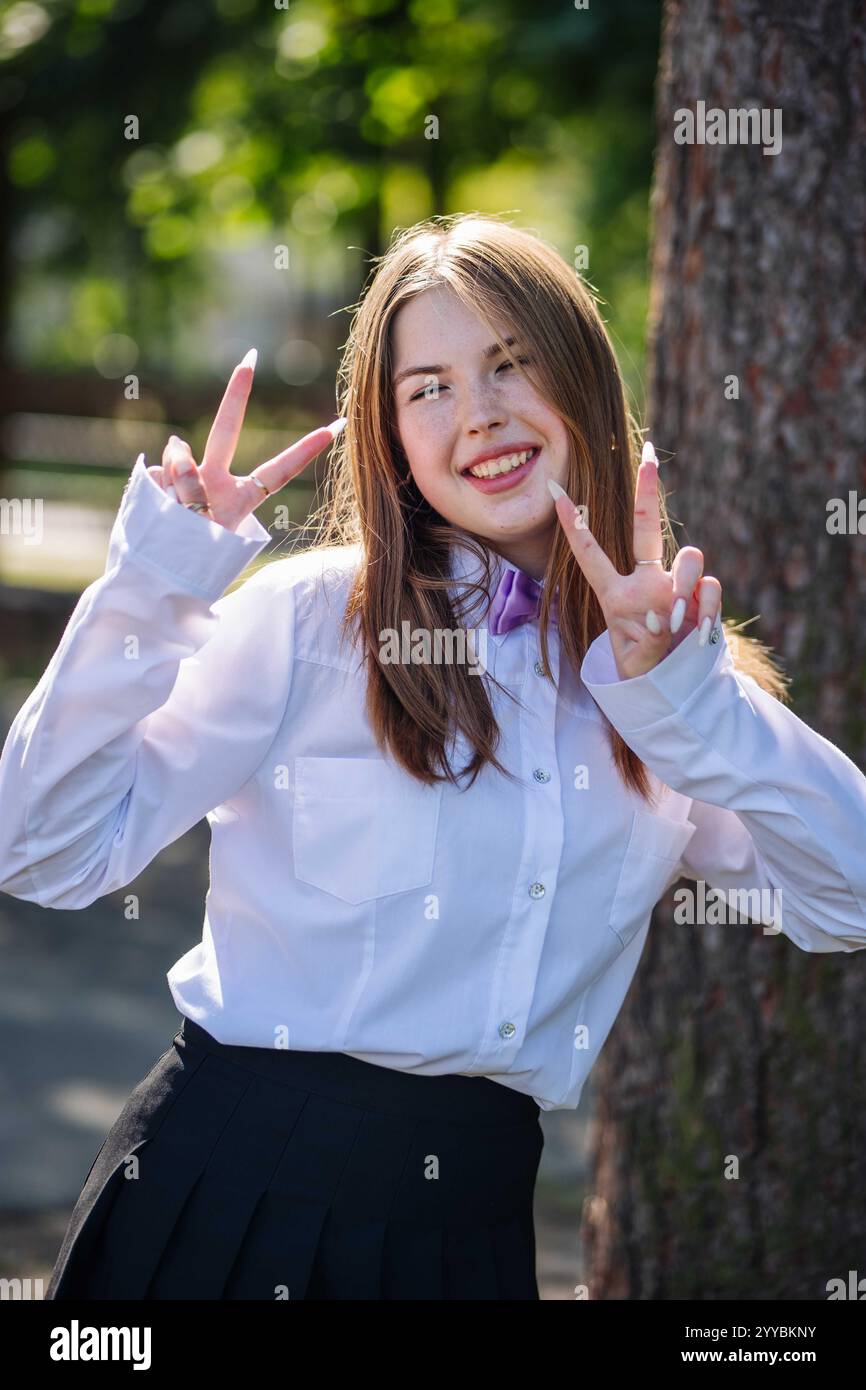 Happy student wearing white shirt and black skirt showing victory sign ...