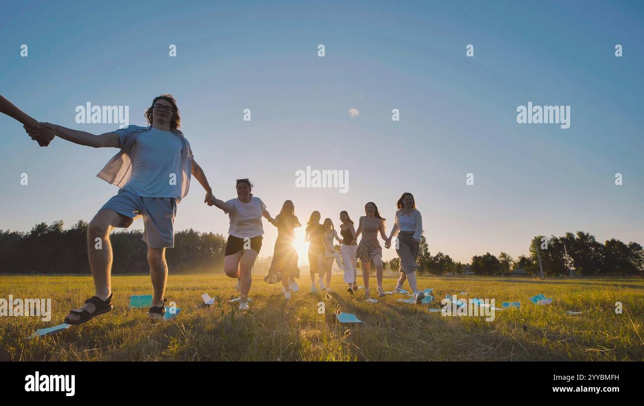 Joyful high school graduates running together in a field at sunset ...