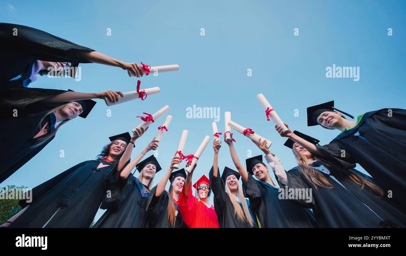 Happy students in academic gowns and graduation caps raising their ...