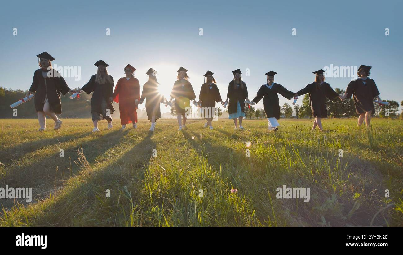 Students in graduation attire walking through a field at sunset ...