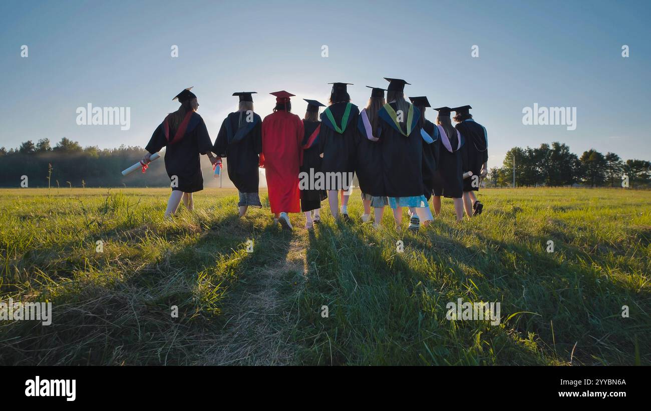 Graduating students walking through a field at sunset, proudly holding ...