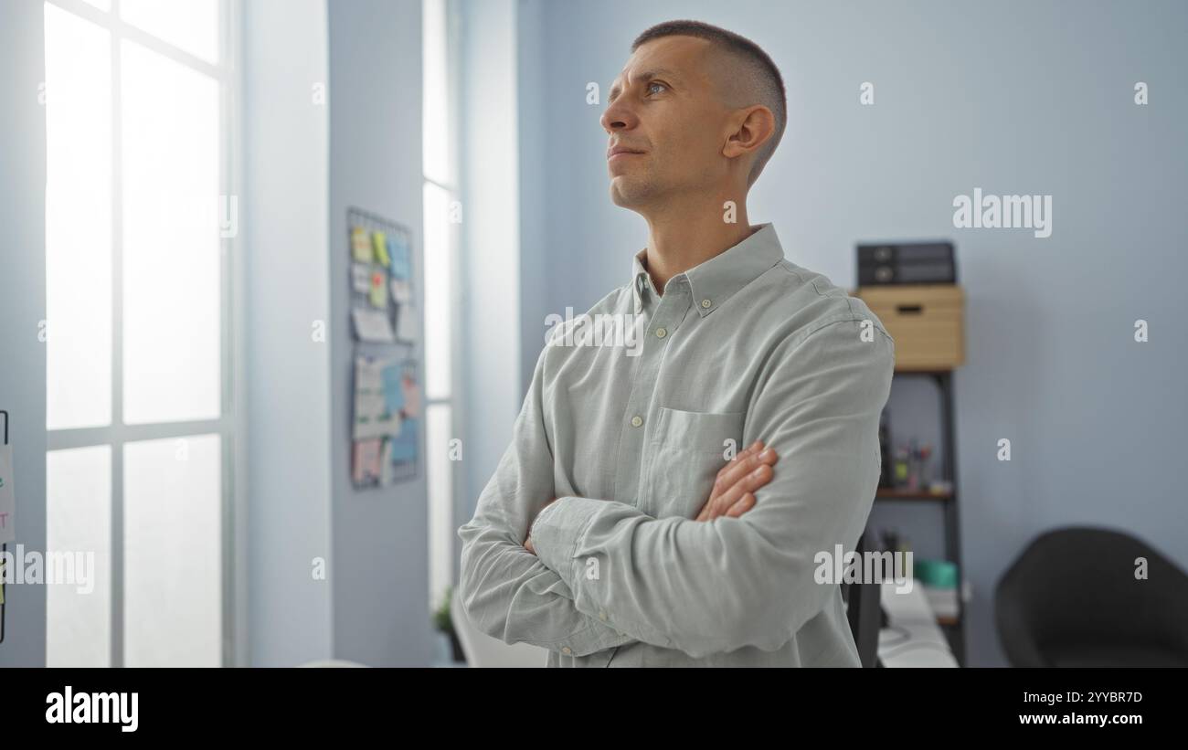 Young man in an office stands confidently with arms crossed, looking ...