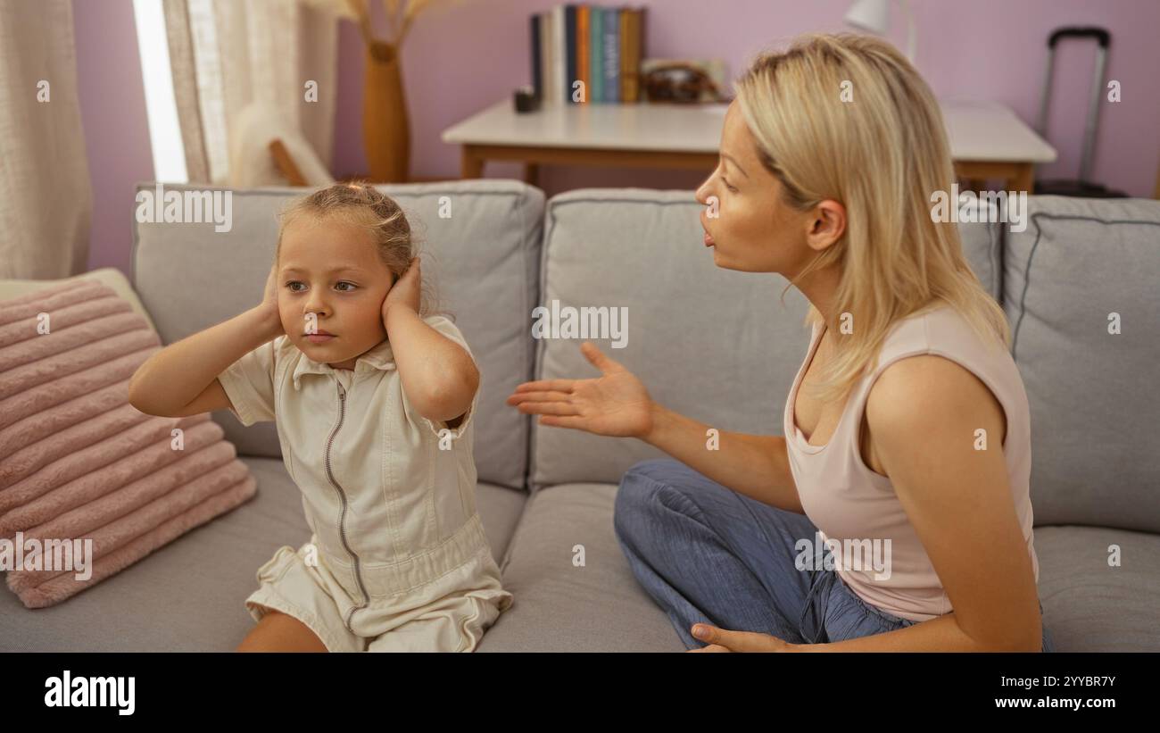 Mother talking while daughter covers ears on a couch in living room ...