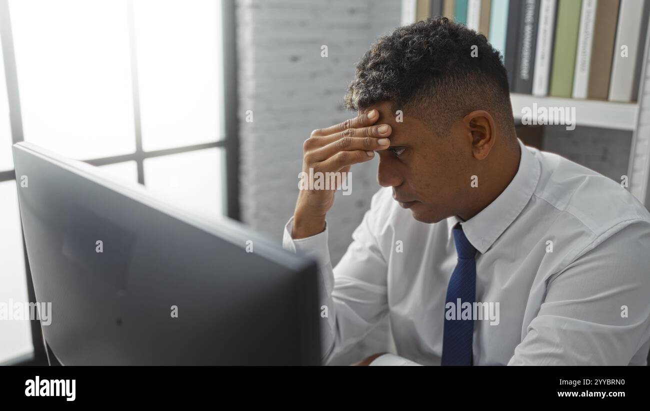 Young man sitting in an office looking at his computer screen with a ...