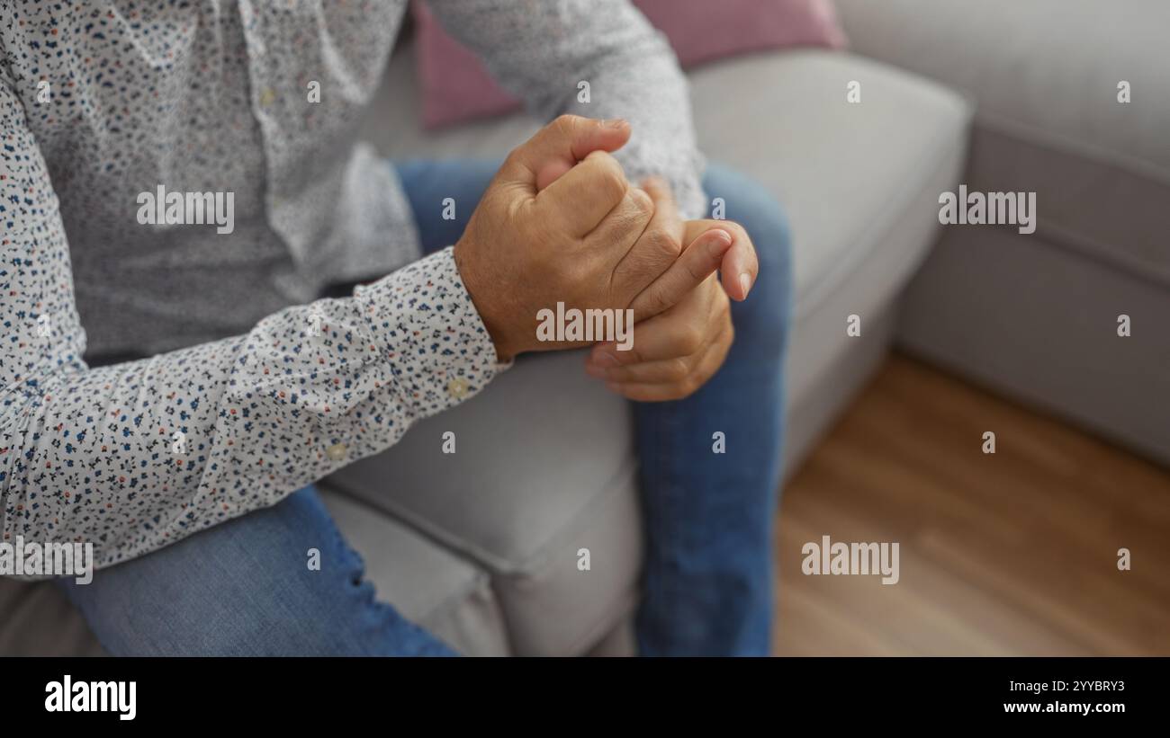 A hispanic man sitting indoors in a living room with his hands clasped ...
