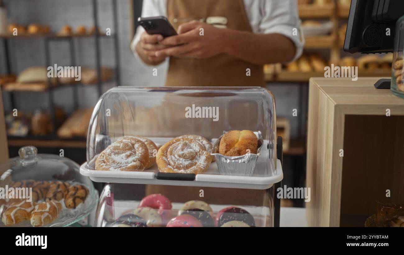 Young man holding smartphone behind bakery counter with pastries ...