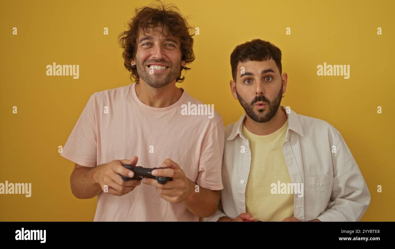 Men smiling together in front of a yellow wall, one holding a game ...