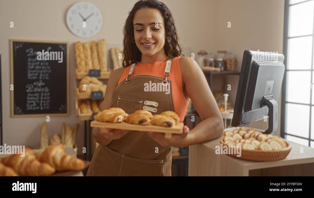 Young woman holding pastries inside a bakery shop with a smile on her ...