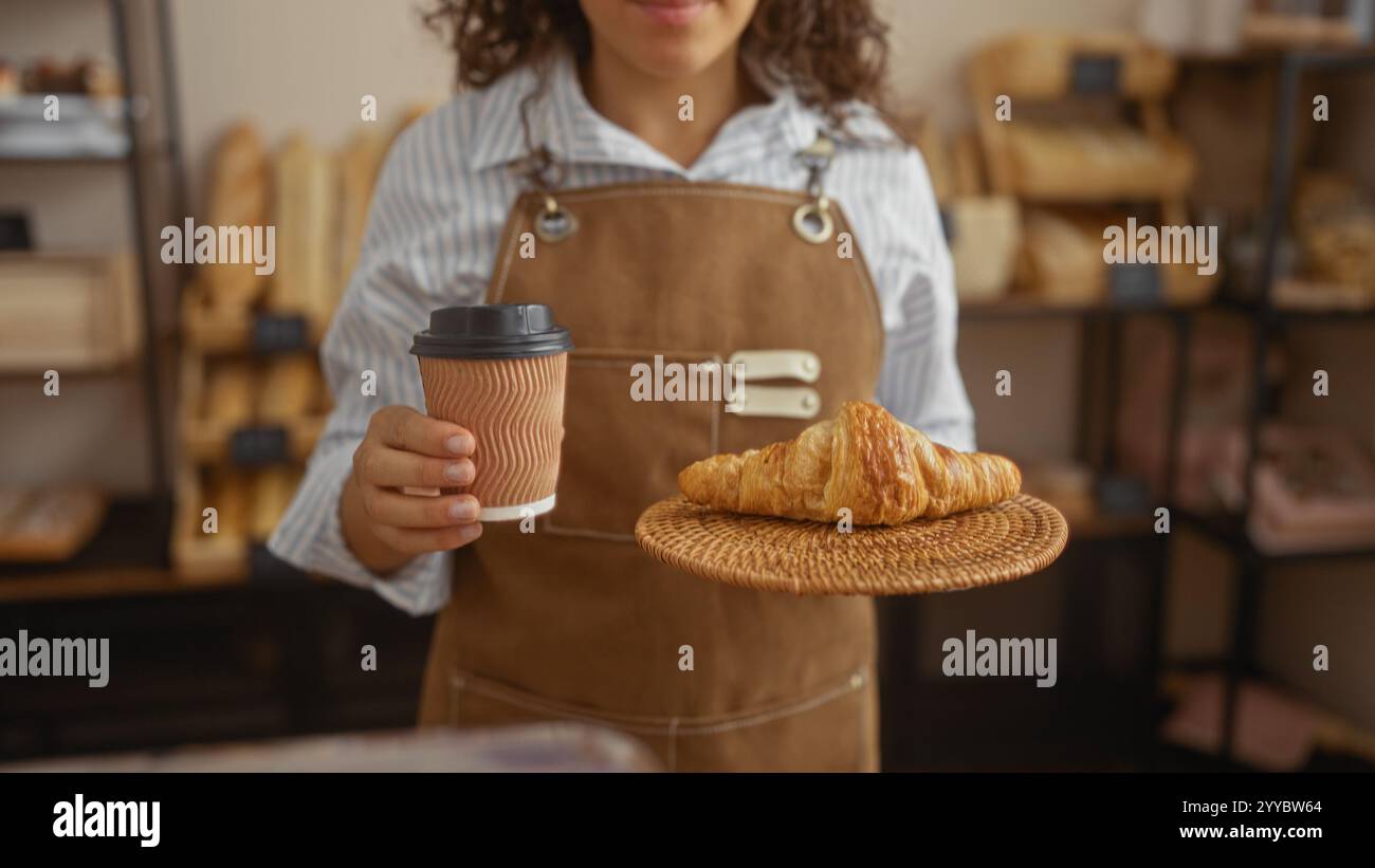 Hispanic woman holding coffee and croissant indoors at a bakery ...