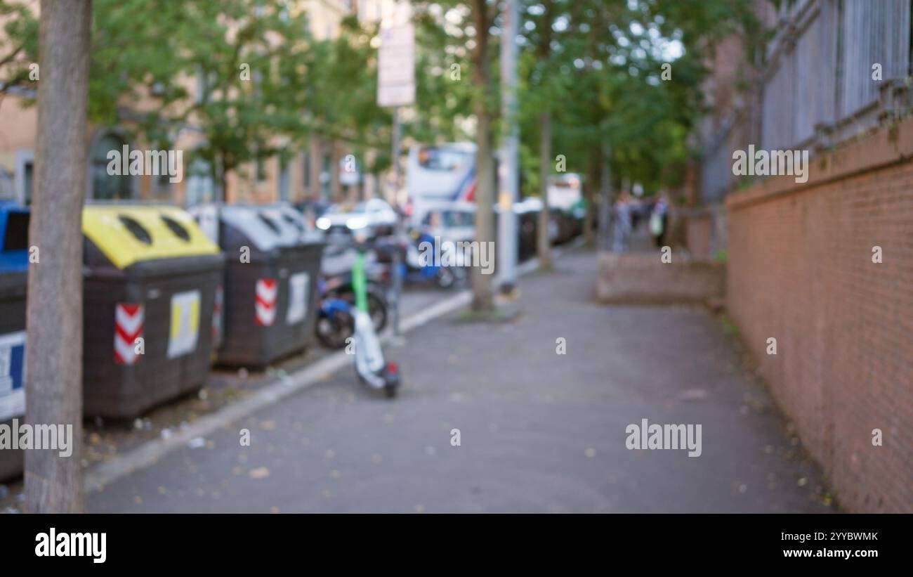 Defocused urban street scene featuring blurred rubbish containers and ...