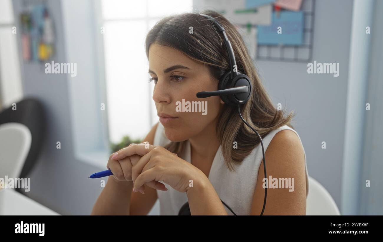 Young woman focused in conversation wearing headset and pen in hand in ...