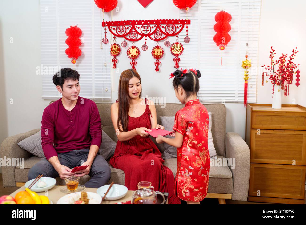 A child joyfully receives a red envelope (angpao) from parents during a ...