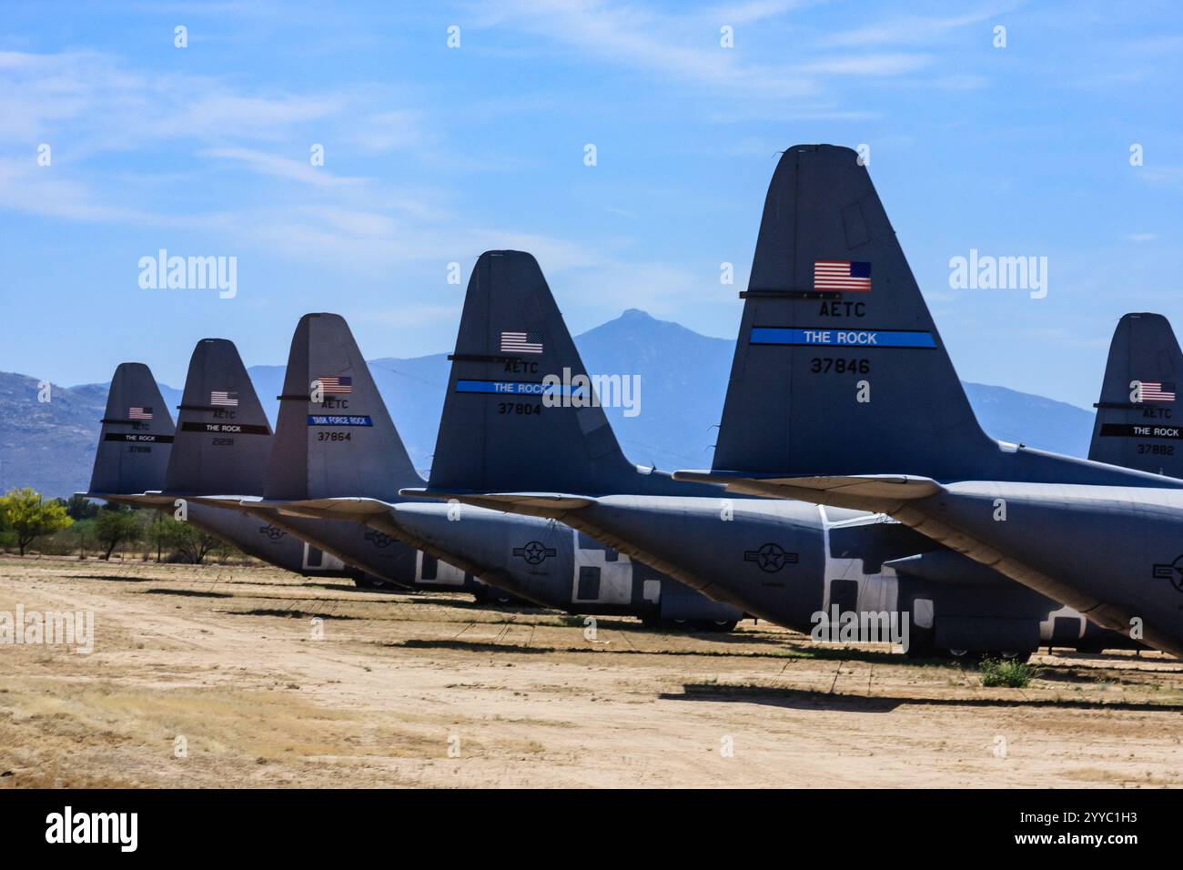 A row of military planes are parked in a desert. The planes are all ...