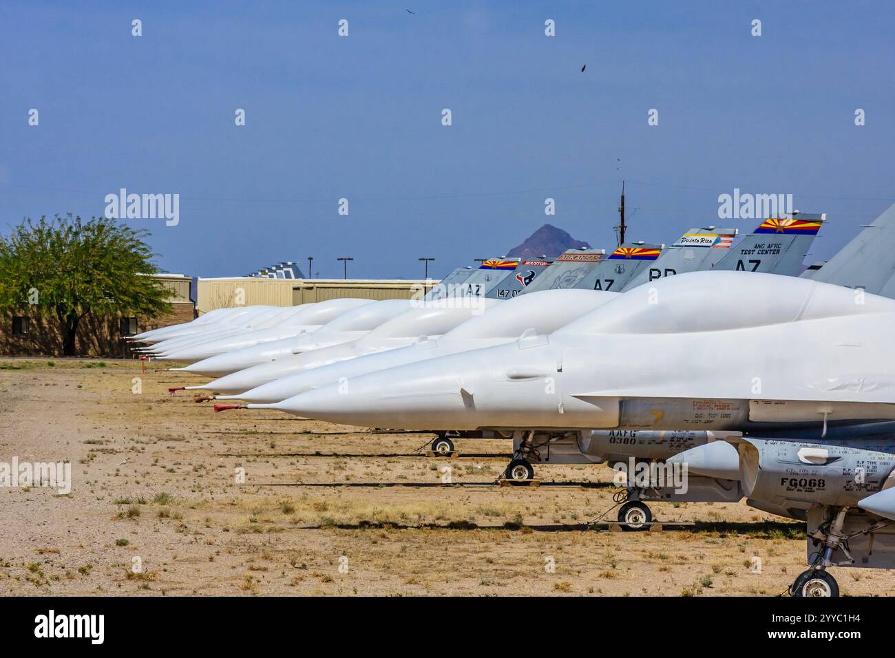 A row of fighter jets are parked in a desert. The planes are white and ...